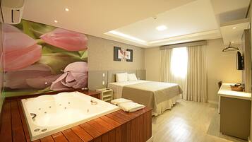 Quarto de hotel com uma banheira grande, uma cama, uma escrivaninha e um espelho.