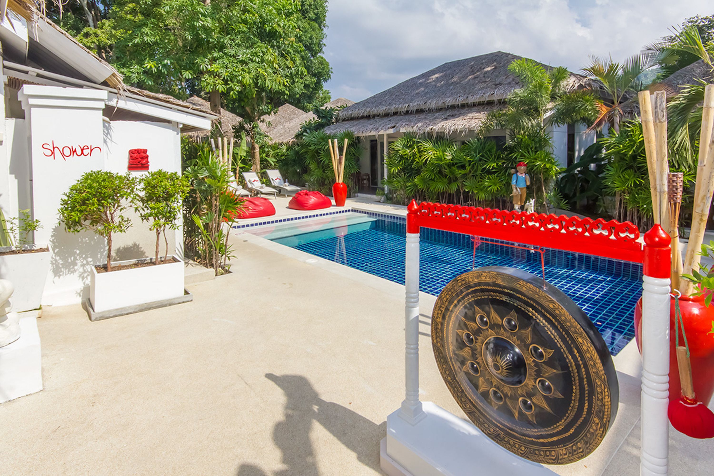 Uma área de piscina com cerca vermelha e branca, um portão decorativo e cadeiras de lounge.