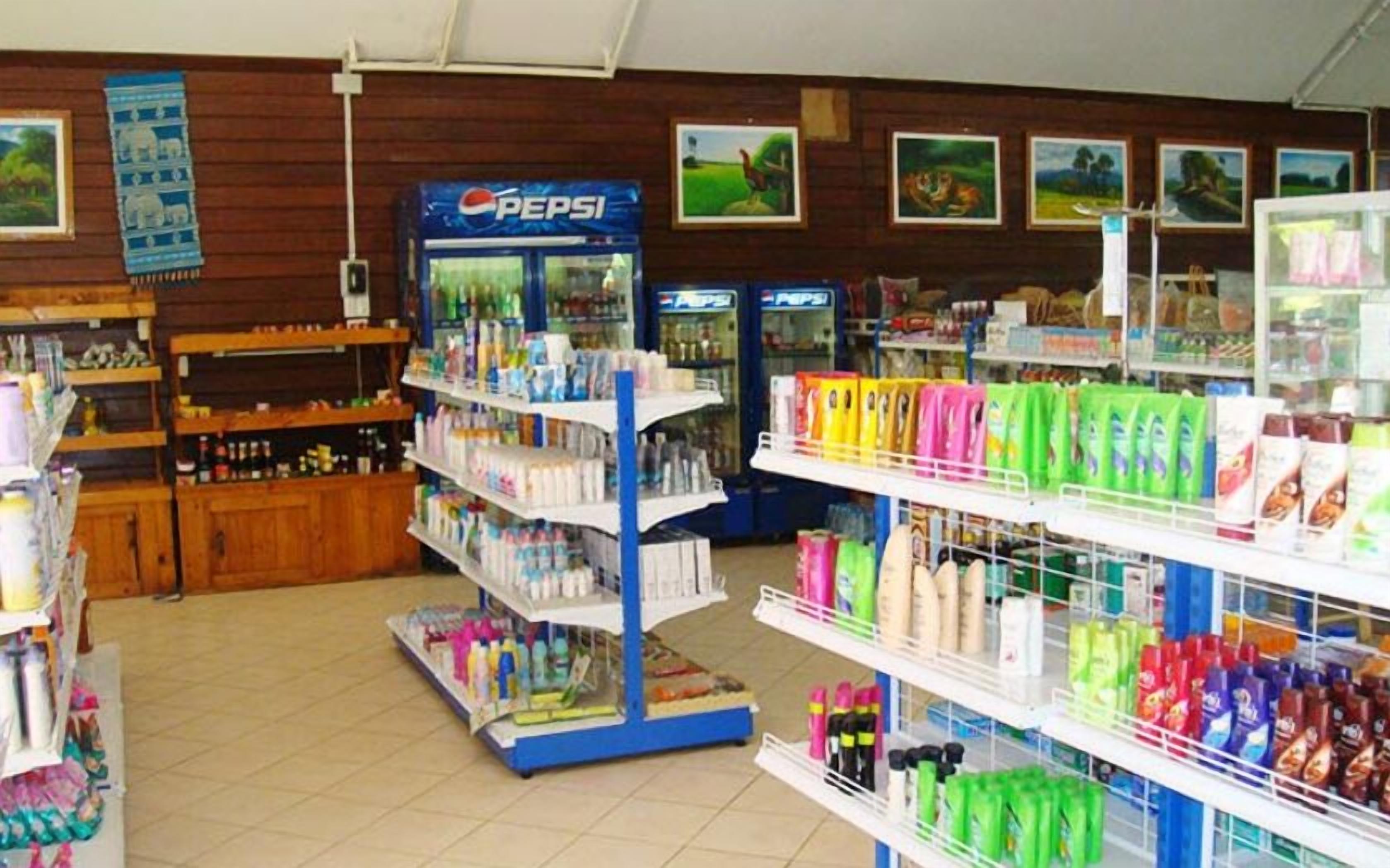Interior de loja com prateleiras repletas de diversos produtos, incluindo um refrigerador da Pepsi.