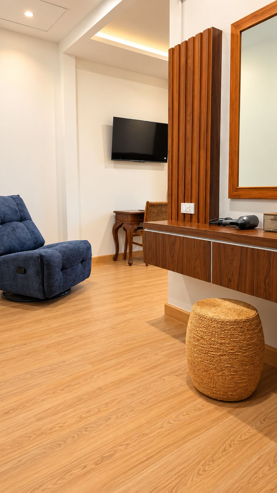 Quarto moderno com sofá azul, armário de madeira, televisão e um banquinho de vime.
