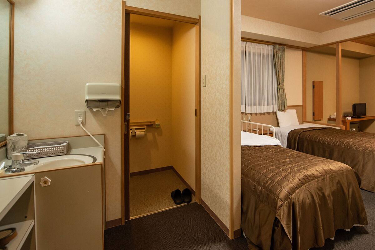 Quarto de hotel com banheiro, duas camas, uma escrivaninha e janela com vista.