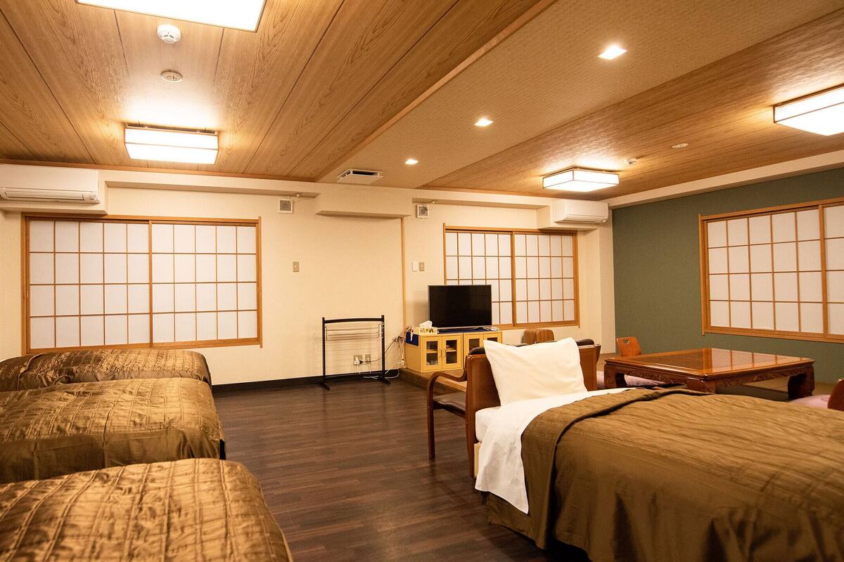 Quarto de hotel com duas camas, televisão, escrivaninha e portas japonesas tradicionais.