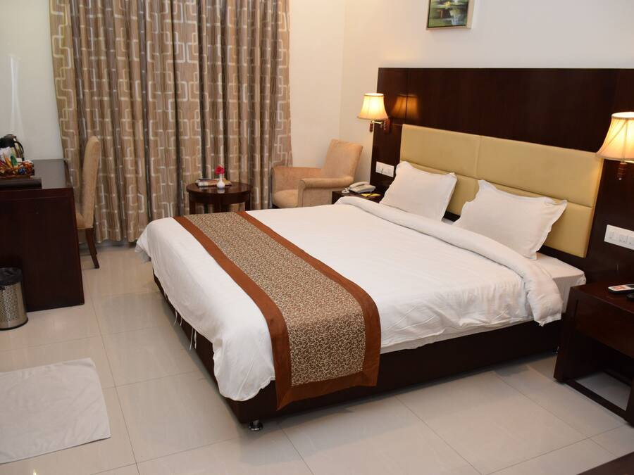 Quarto de hotel com uma cama grande, duas luminárias de cabeceira, uma cadeira, uma mesinha e um cesto de lixo.