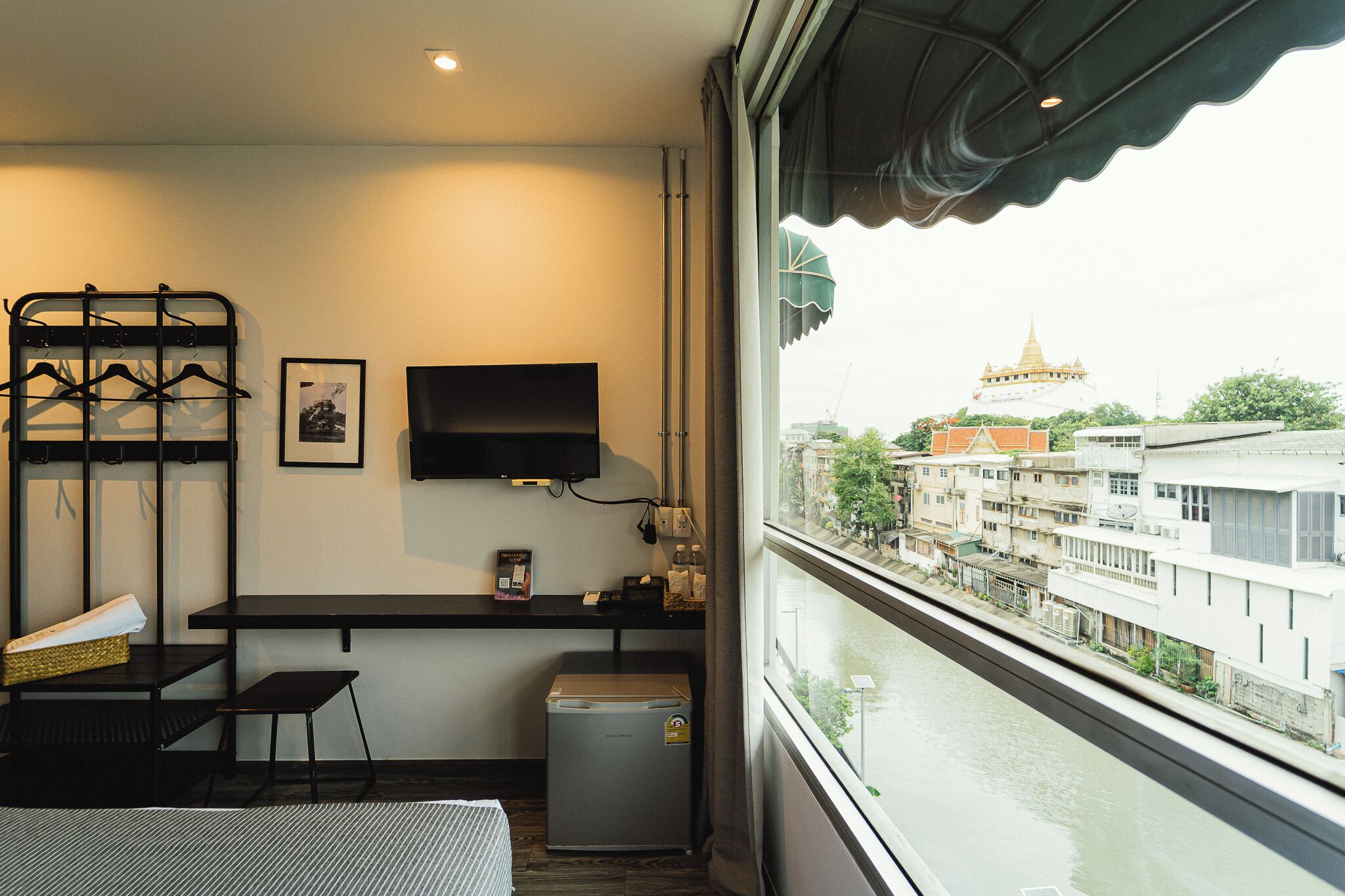 Quarto de hotel com cama, escrivaninha, televisão, mini-geladeira e vista para a paisagem urbana com um templo dourado.