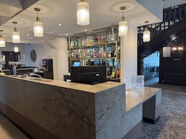 Uma área de bar com balcão de mármore, várias garrafas de bebidas e um monitor de computador.
