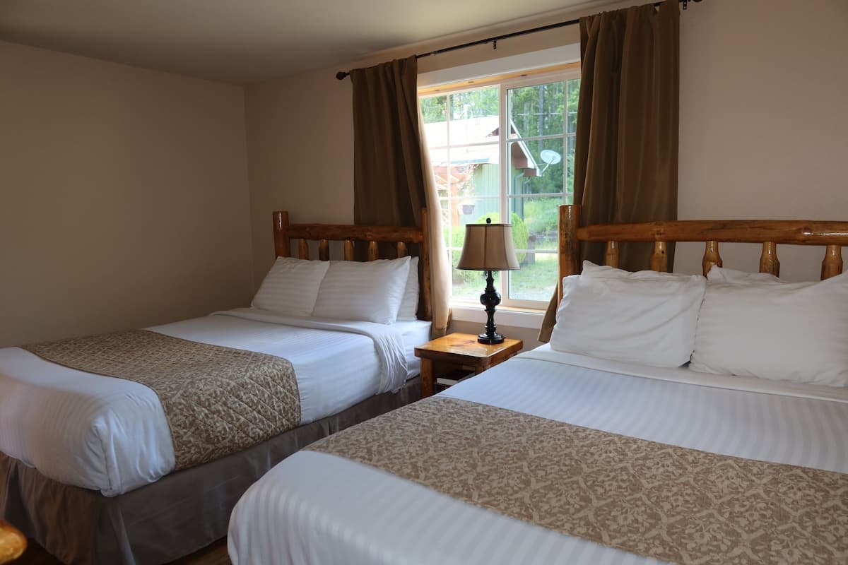 Quarto com duas camas, mesa de cabeceira com abajur e janela com cortinas.