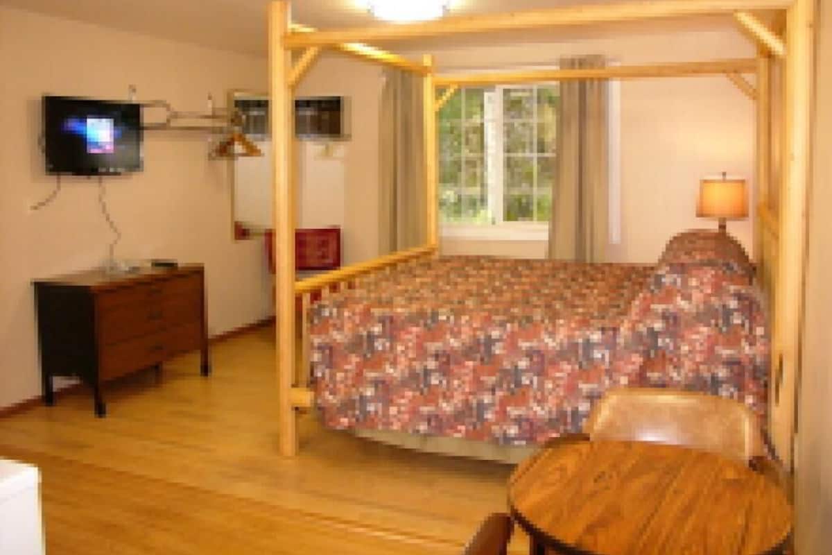 Quarto com uma cama de dossel de madeira, televisão na parede, uma escrivaninha e uma janela com cortinas.