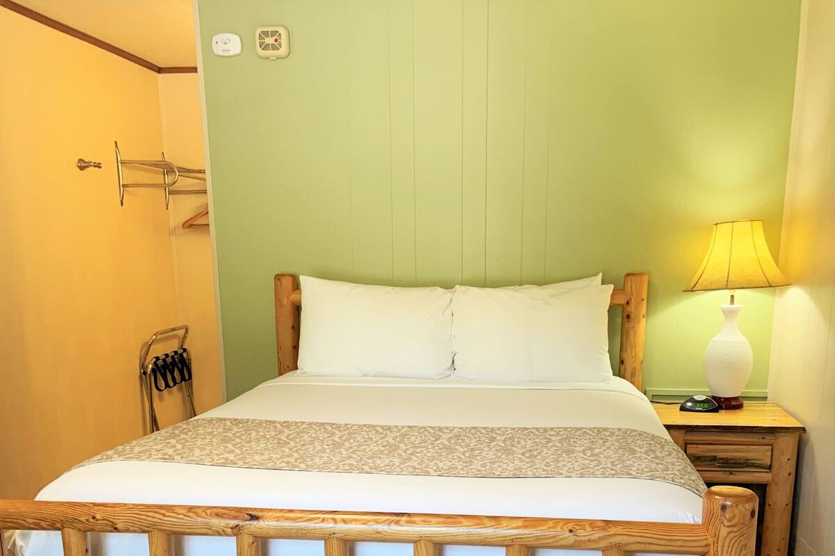 Uma cama com estrutura de madeira, cabeceira e mesa de cabeceira com abajur.