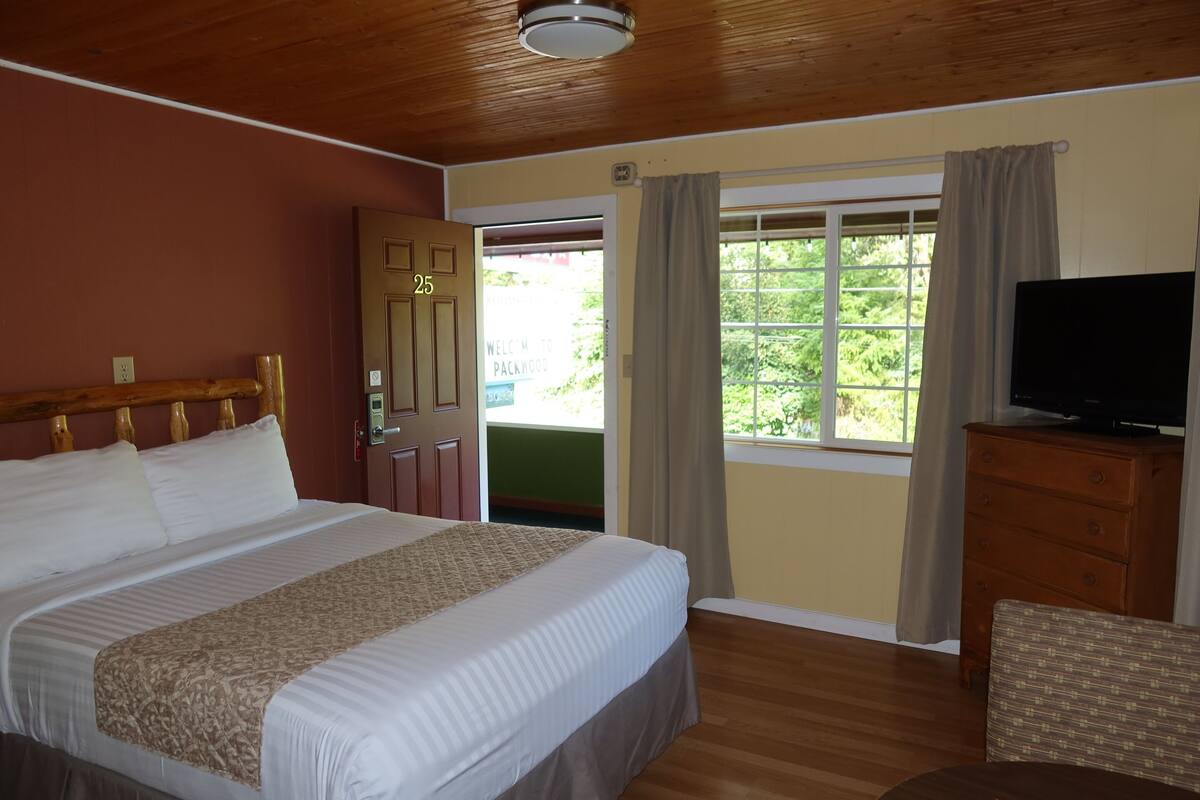 Quarto de hotel com uma cama, televisão, cómoda de madeira e janela com cortinas.