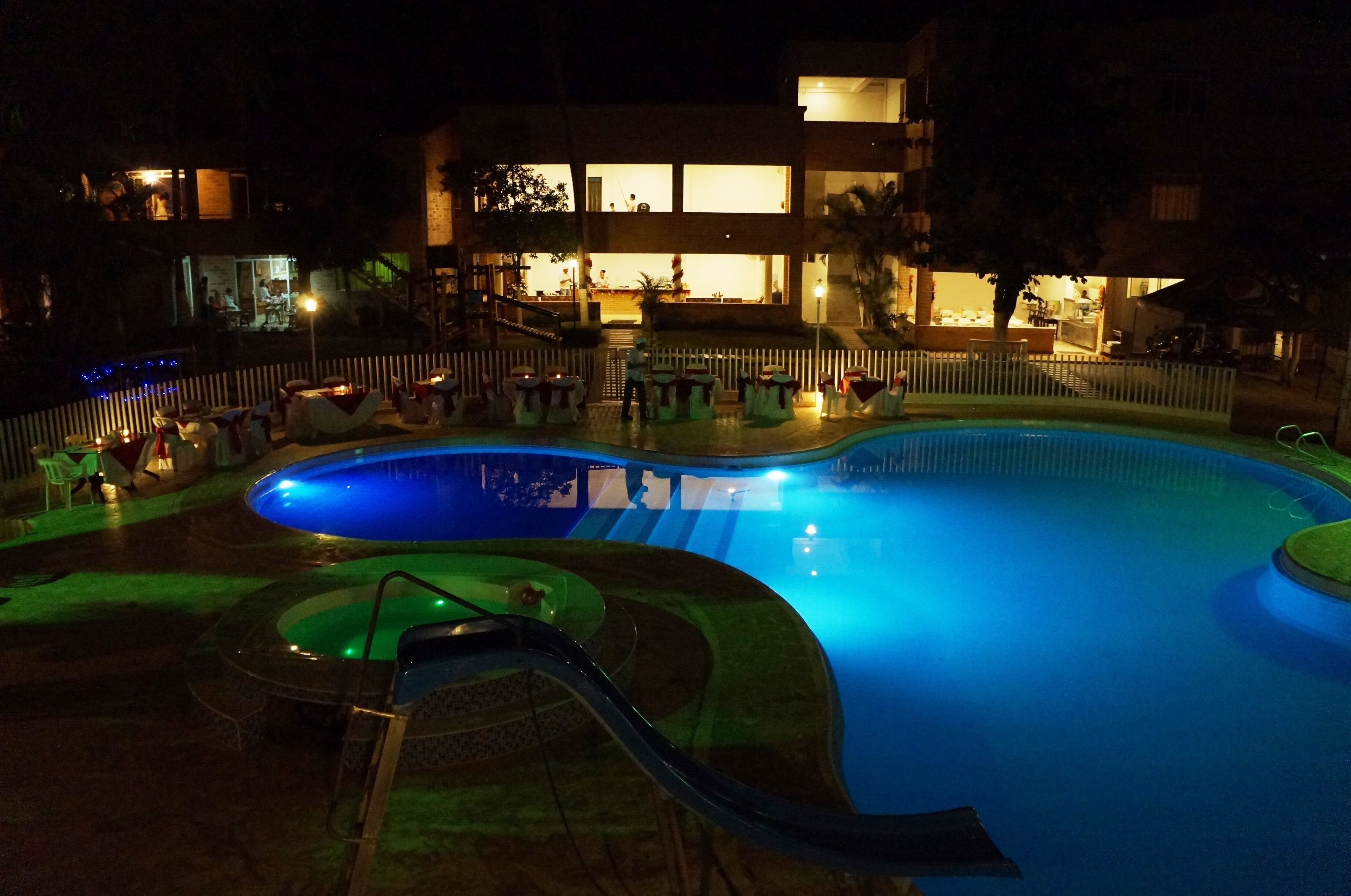 Uma piscina com escorrega, cercada por um muro branco e área de estar ao ar livre.