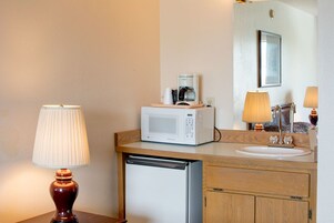 Uma casa de banho de hotel com uma toucador de madeira, uma pia branca, um micro-ondas, uma máquina de café e um candeeiro.