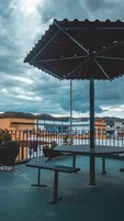 Terraço no telhado com guarda-sol de metal, área de estar e plantas em vasos.