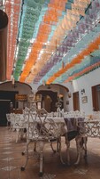Uma sala de jantar com cadeiras e mesas brancas ricamente decoradas, adornada com lanternas de papel coloridas.