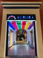 Entrada de hotel com uma placa indicando "AURORA" e decorações pendentes coloridas.