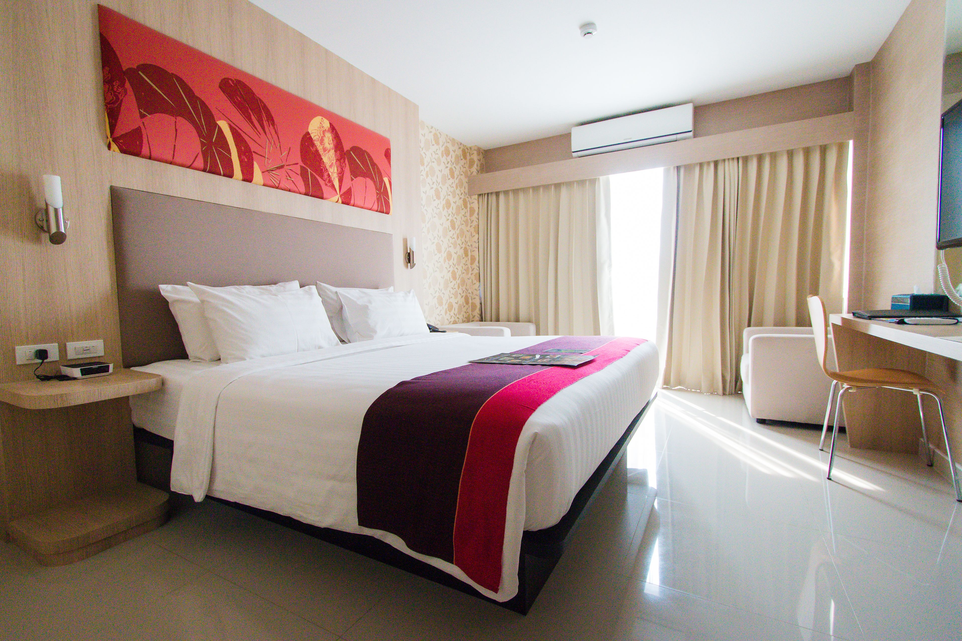 Quarto de hotel com uma cama grande, uma escrivaninha, uma cadeira e uma televisão.