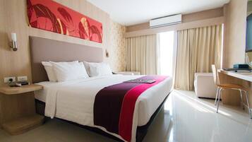Quarto de hotel com uma cama grande, uma escrivaninha, uma cadeira e uma televisão.