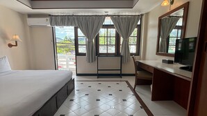 Quarto de hotel com cama, escrivaninha, televisão e janela com cortinas.