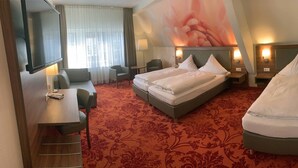 Quarto de hotel com uma cama grande, uma escrivaninha, uma cadeira, uma televisão e uma grande obra de arte floral na parede.