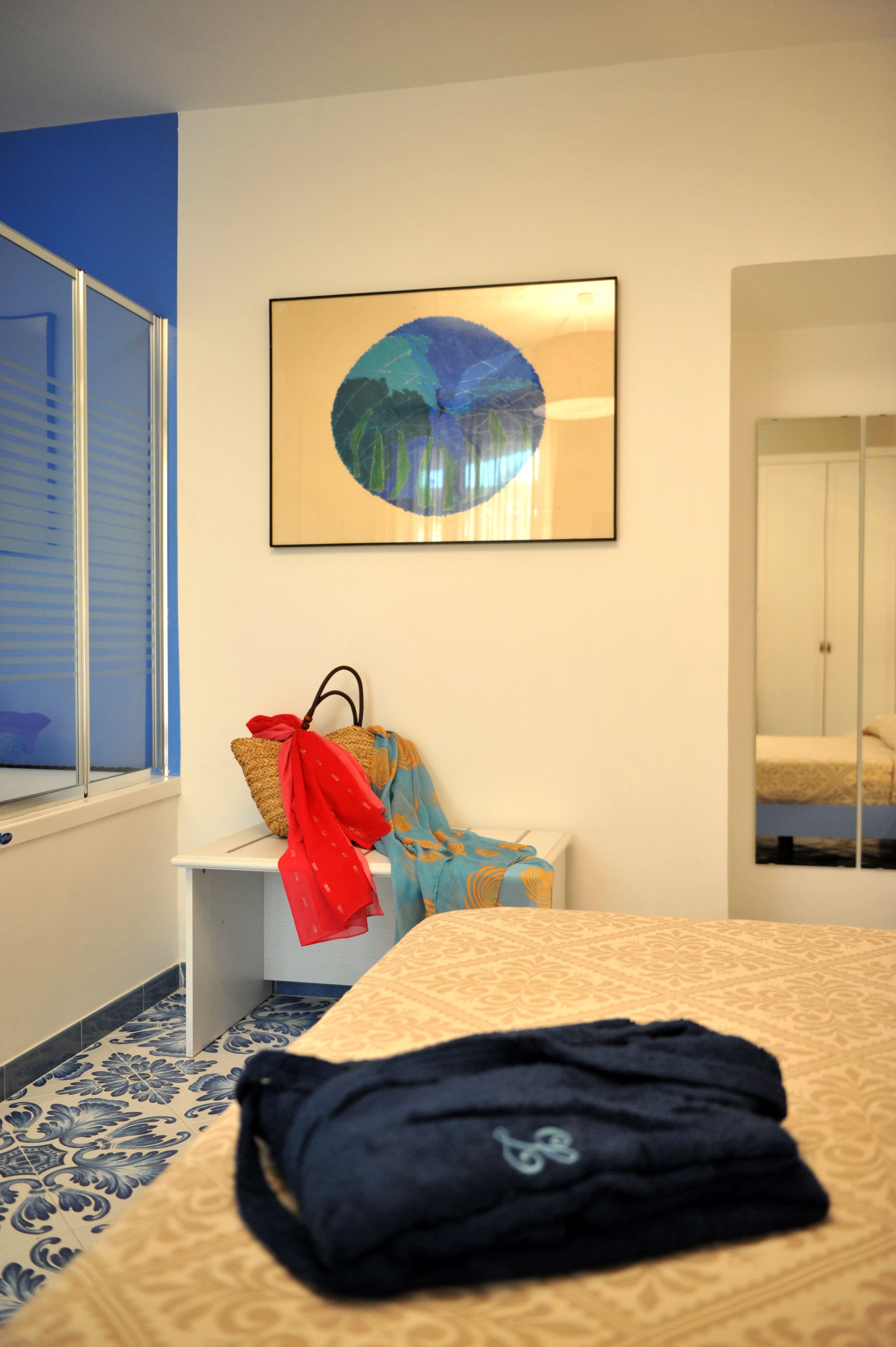 Quarto de hotel com cama, cadeira, janela com persianas, uma obra de arte na parede e mala no chão.