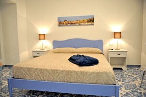 Quarto com uma cama, duas mesas de cabeceira, um criado-mudo, um quadro na parede e ladrilhos de chão estampados.