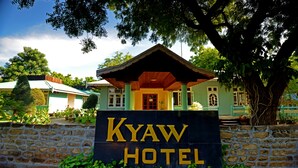Placa de hotel com o nome 'Kyaw Hotel' e uma parede de pedra com vegetação à frente.