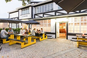 Uma área externa com mesas e bancos amarelos, um edifício com a inscrição 'St Andrews Accommodation' ao fundo, e um bar visível pela entrada.