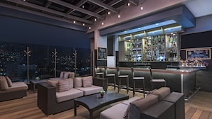 Um bar no terraço com balcão, área de estar e vista para a cidade.