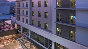 Um hotel de vários andares com design moderno, exibindo uma placa chamativa 'Hyatt Place', um átrio de vidro e vista para a paisagem urbana.