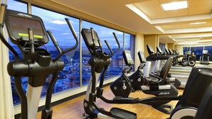 Uma academia com vários equipamentos de cardio, grandes janelas e vista para a cidade.