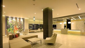 Um hall moderno com balcão de recepção, área de estar e uma grande obra de arte abstrata.