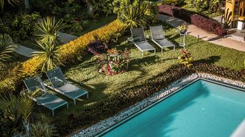 Uma área de piscina com espreguiçadeiras, piscina e paisagismo bem cuidado.