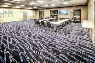Sala de conferências com carpete estampado, mesas e cadeiras brancas.