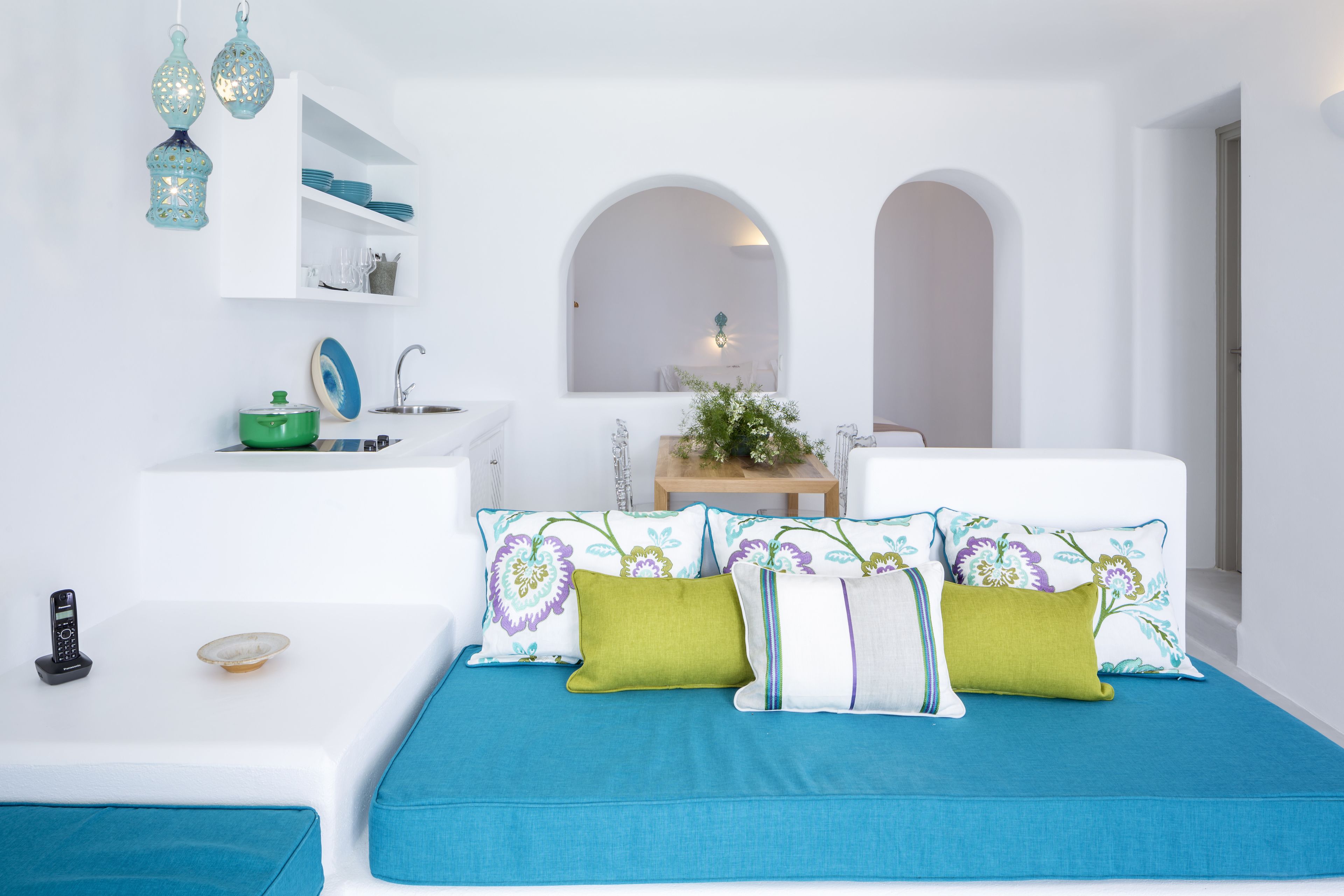 Quarto moderno com decoração em tons de branco, uma cama, mesa de cabeceira e um pequeno espaço de estar.