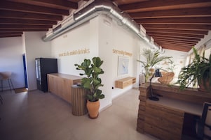 Interior moderno com balcão de recepção de madeira, planta em vaso e parede com a inscrição "snacks & cold drinks" e "serenity lounge".