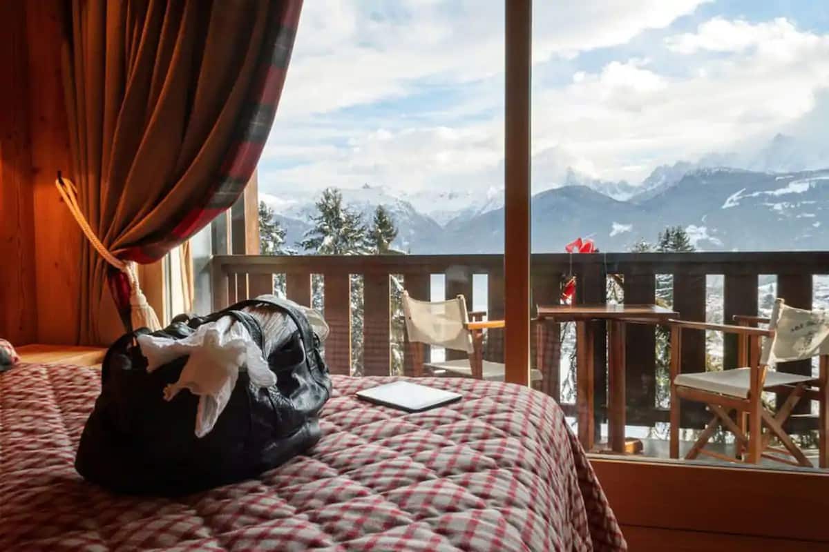 Quarto de hotel com cama, mala e vista para montanhas.
