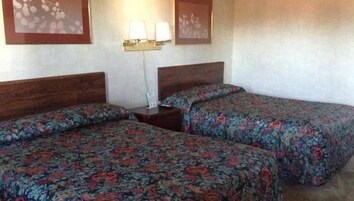 Quarto de hotel com duas camas, cada uma com roupa de cama florida, mesa de cabeceira com abajur e quadros com flores nas paredes.