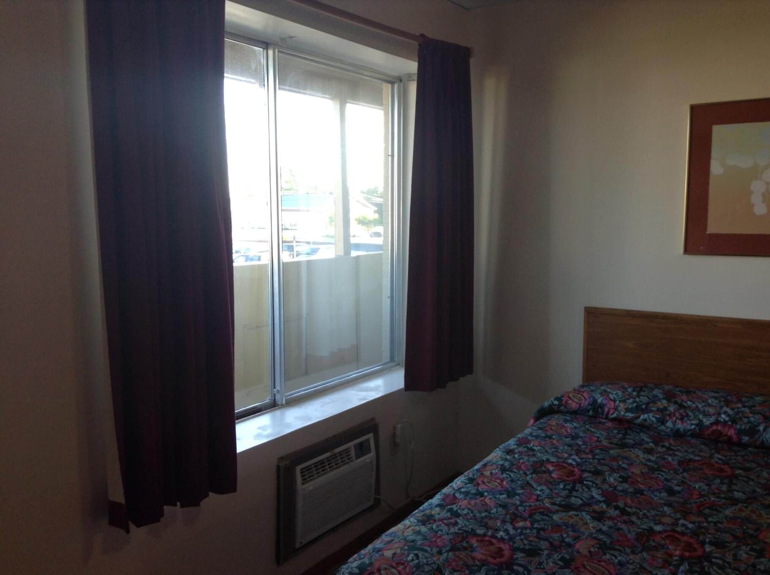 Um quarto com uma cama, uma janela com cortinas e um radiador.