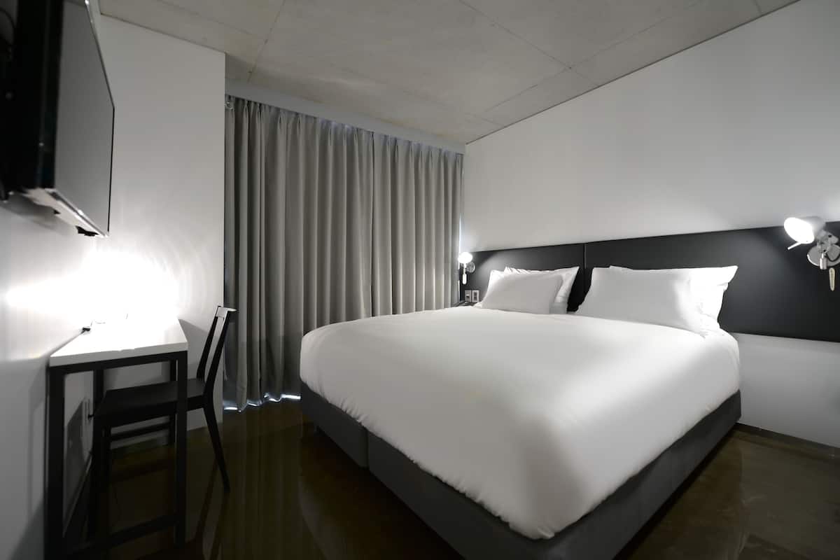 Quarto de hotel moderno com uma cama grande, uma escrivaninha com cadeira e uma TV de tela plana.