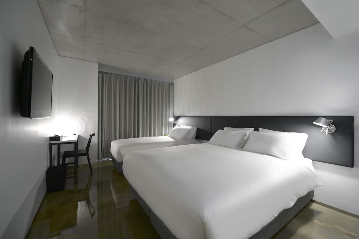 Quarto de hotel moderno com uma cama grande, uma escrivaninha e uma televisão de tela plana.