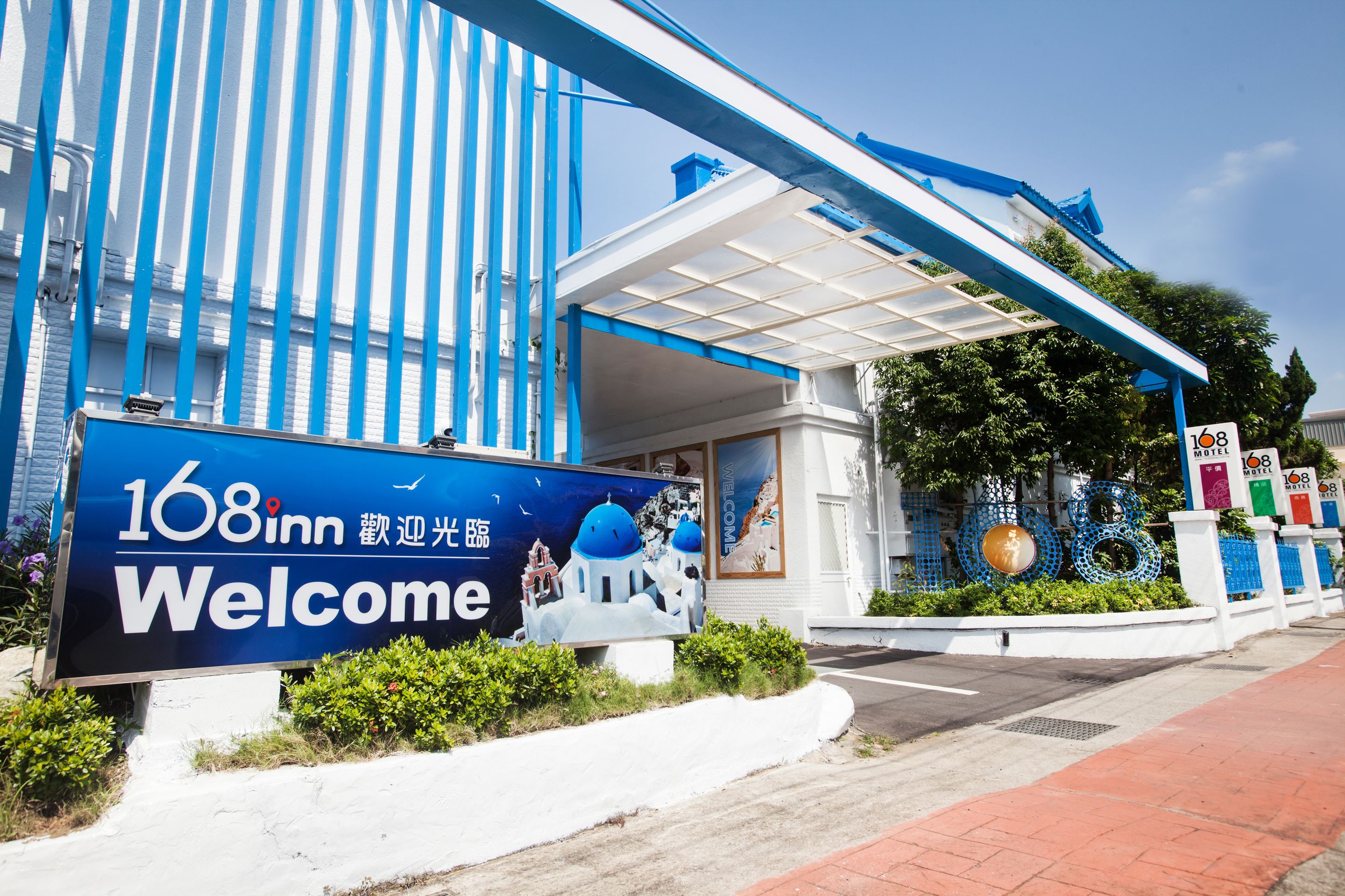 Entrada de um hotel 168inn, com esquema de cores azul e branco, uma placa de identificação e uma cerca decorativa.