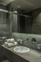 Uma casa de banho moderna com chuveiro em cabine de vidro, lavatório branco e espelho.