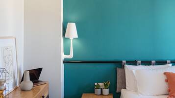 Quarto moderno com uma parede de destaque em tons de verde-água, uma escrivaninha de madeira, uma cama com roupa de cama branca e uma pequena mesa de cabeceira com uma luminária.