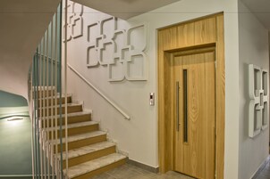 Uma escada com corrimão, uma porta de madeira e interruptores de luz fixados na parede.