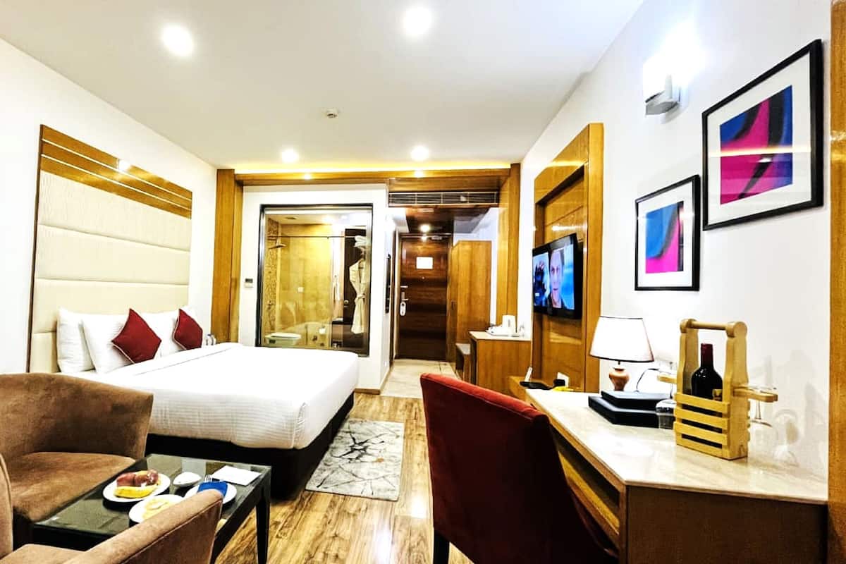 Quarto de hotel com cama, escrivaninha, cadeira, televisão e minibar.