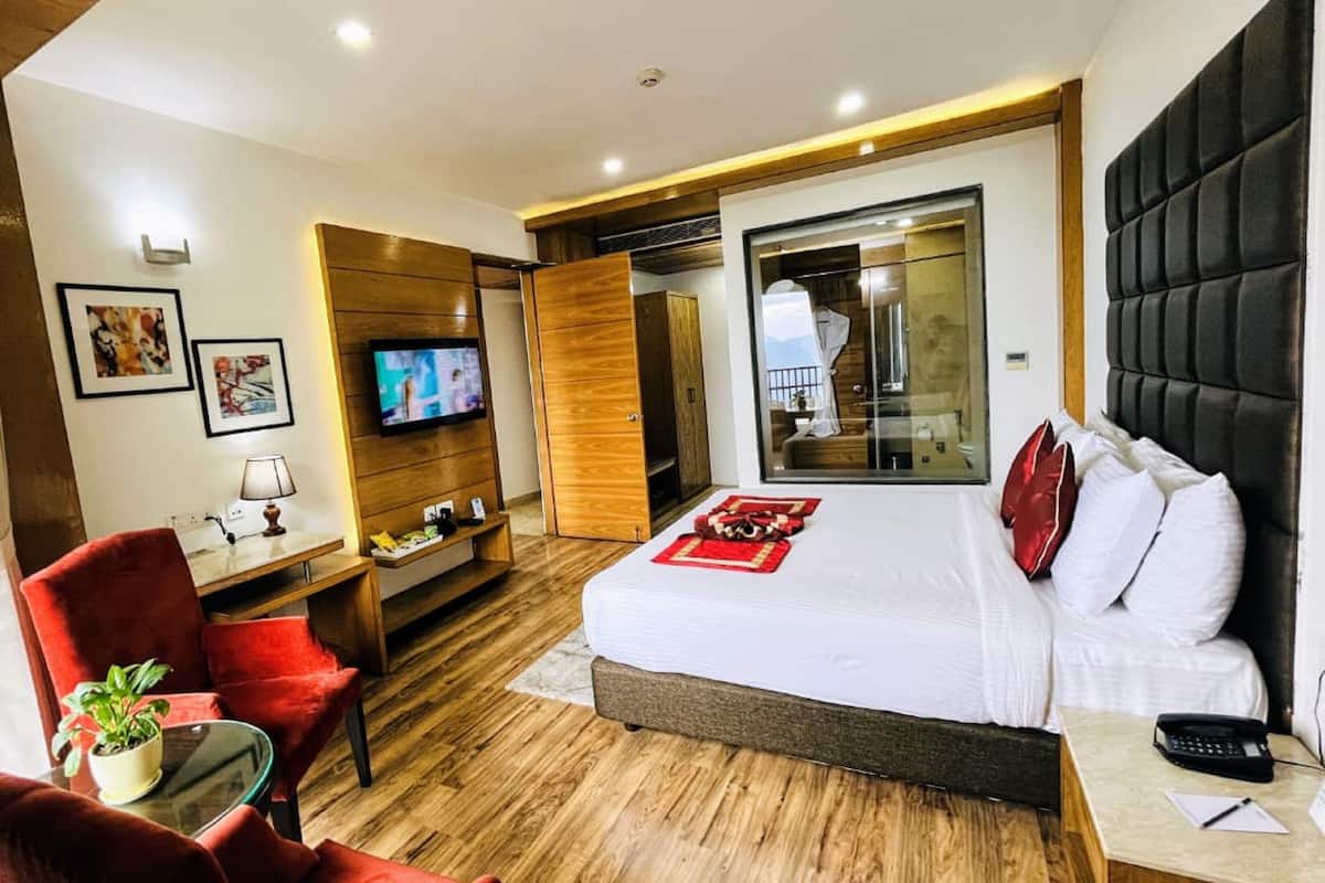 Quarto de hotel moderno com cama, escrivaninha, televisão e área de estar com uma planta.