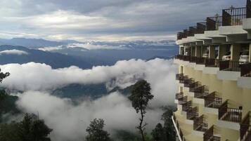 Hotel com várias varandas com vista para uma paisagem montanhosa e nuvens abaixo.