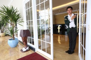 Entrada de um hotel com porta de vidro, um vaso de planta e um tapete vermelho.