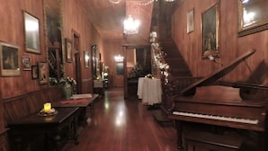 Um hall imponente com um piano de cauda, painéis de madeira, lustres e obras de arte emolduradas nas paredes.