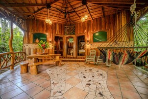 Interior em madeira com piso de azulejos, um banco, uma rede e vista para o exterior.