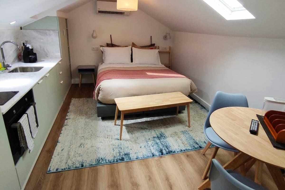 Quarto compacto e moderno com cama estilo loft, mesa de jantar pequena e cozinha compacta.